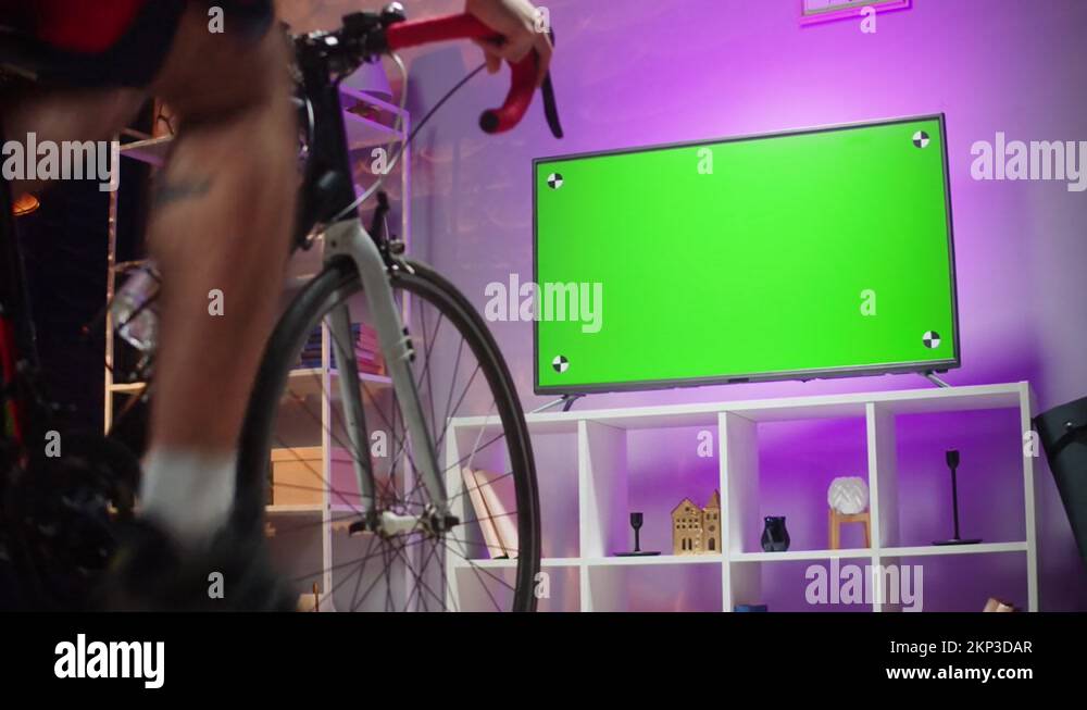 Sportsman riding bicycle and watching tv, home gym. Young man cycling ...