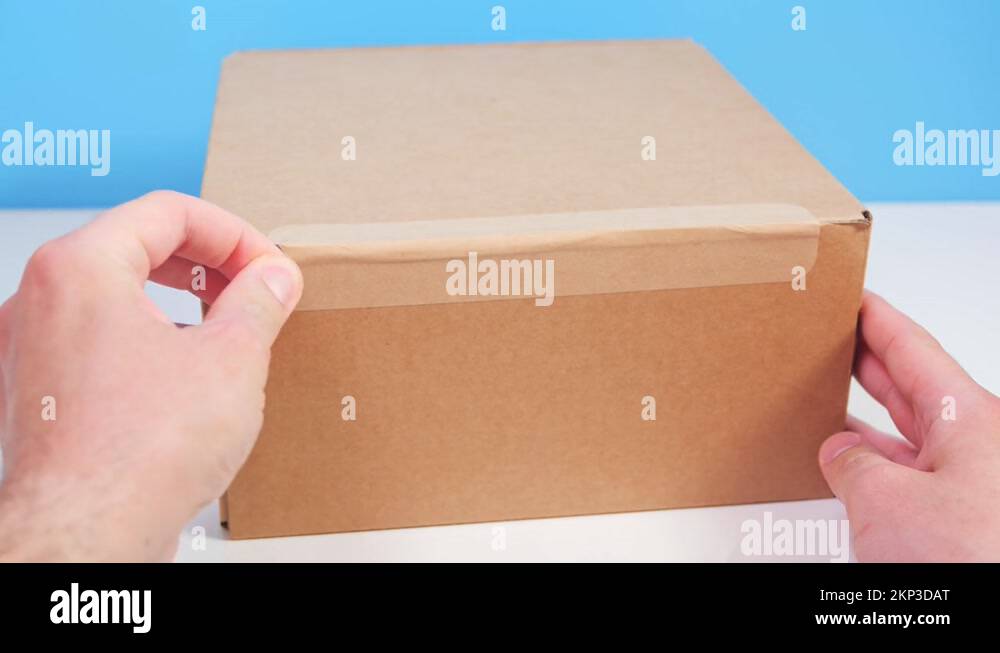 Close up man hand's opening cardboard box package by pulling tear tape ...