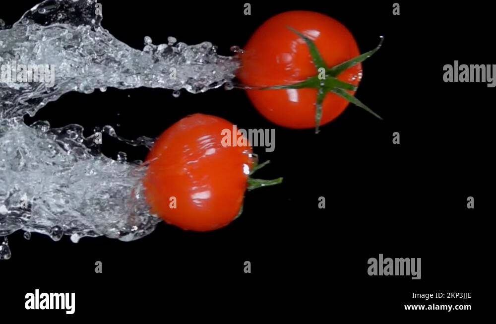 Two small cherry tomatoes are bouncing horizontally on the black ...