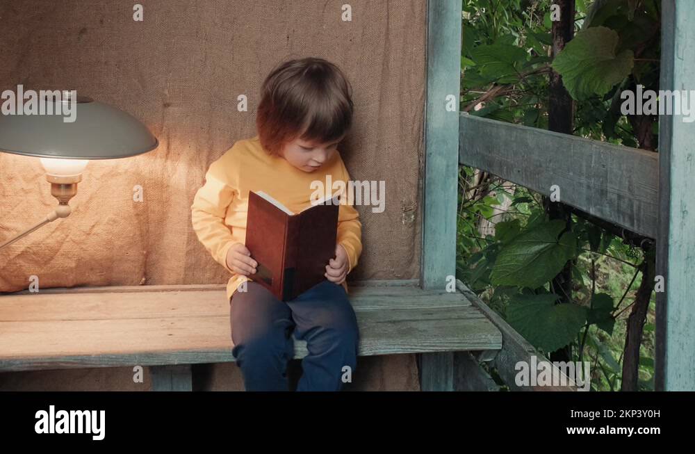 Cute little girl on the porch of a village house is trying to read a ...