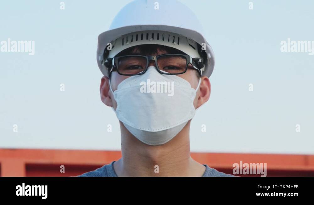 Young Asian engineer wearing a helmet and mask looks and smiles at the ...