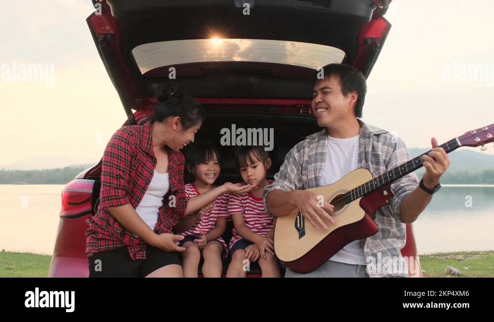 Family sit in the trunk of the car singing along with dad playing the ...