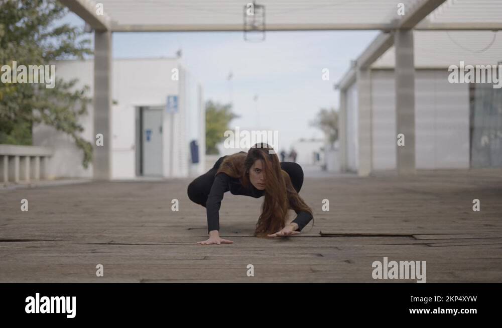Young woman outdoors moves on all fours like a cat, static ground view ...