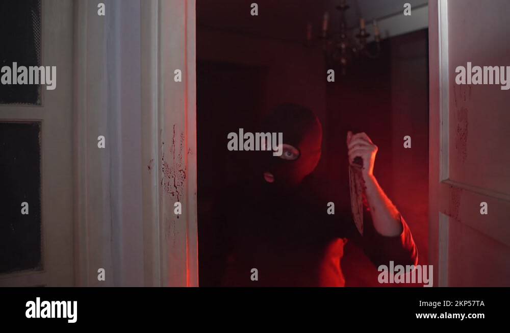 Cruel murderer in balaclava mask haunting his victim with bloody knife ...