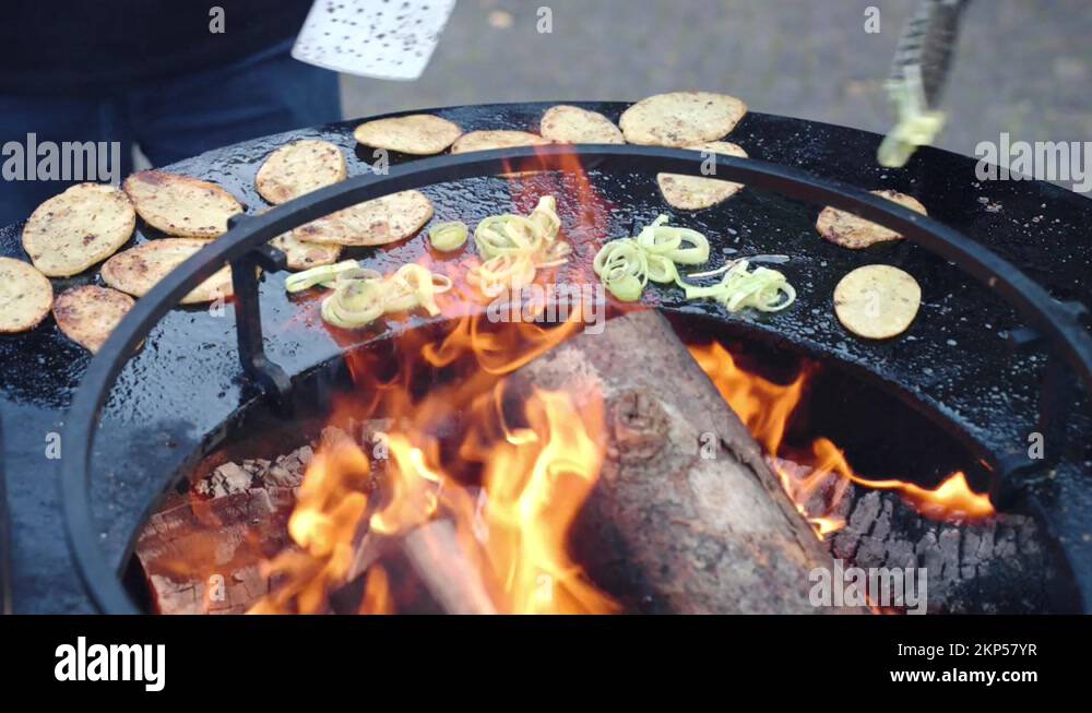 Round black barbecue smoker with burning fire, people roasting potato ...