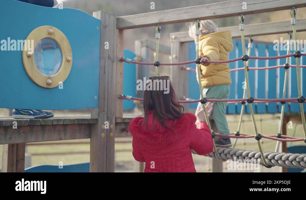 Grandmother overseeing grandson walking over rope bridge in playground ...