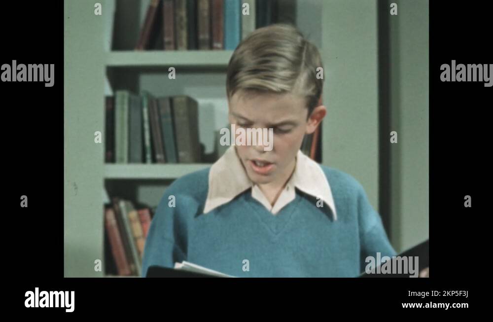 1940s: Blonde boy reads aloud from book. Two boys stand next to seated ...