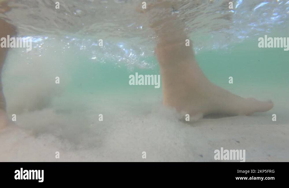 Beautiful underwater clip of feet of an adult walking on shallow beach ...