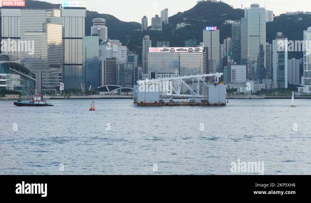 A tug boat is towing a barge in Victoria harbour with the skyline in ...