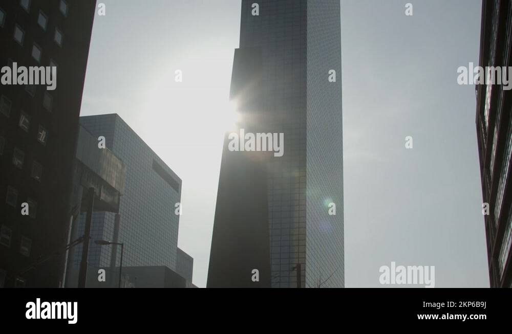 Tilt up of sun shining bright past glass skyscraper in downtown office ...