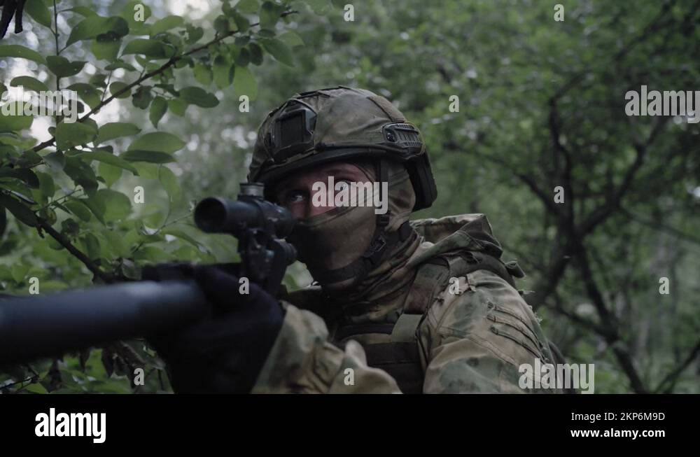 Soldier with sniper rifle, in dense forest, looks into an optical sight ...