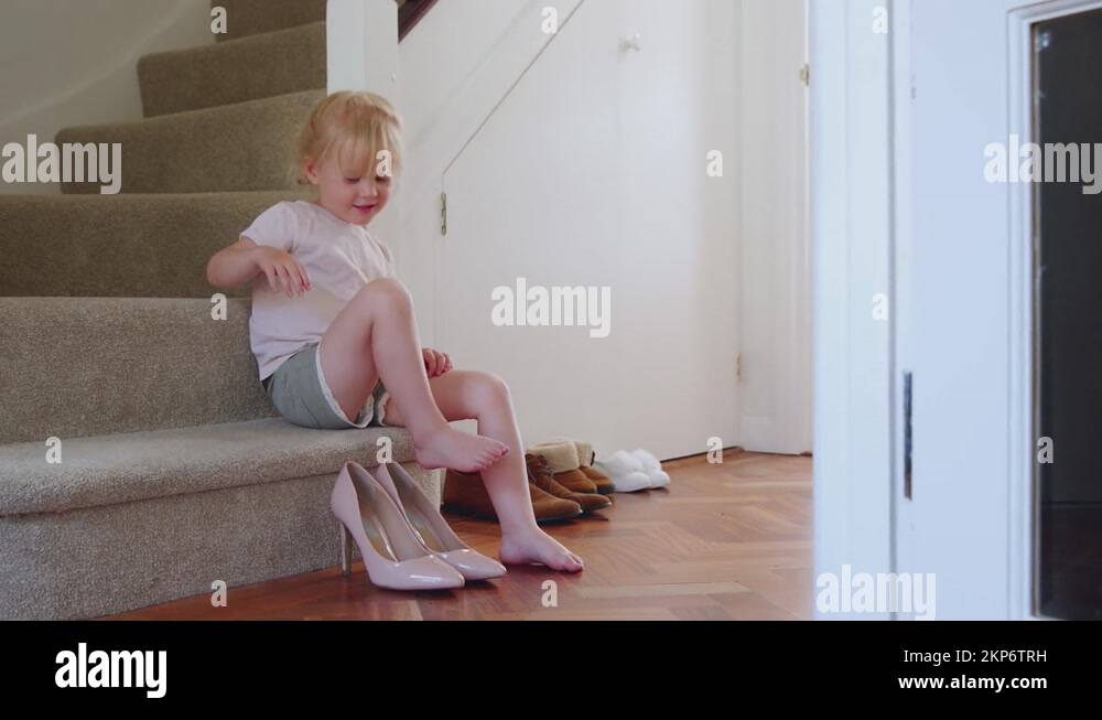 Young girl sitting on stairs dressing up and putting on Mother's high ...