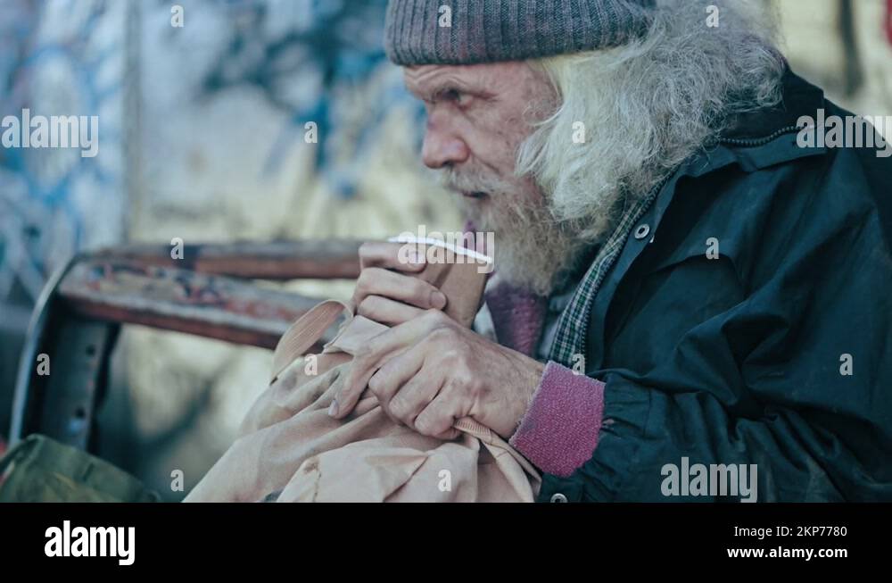 Bearded homeless man searching for drink in his bag, cautiously looking ...