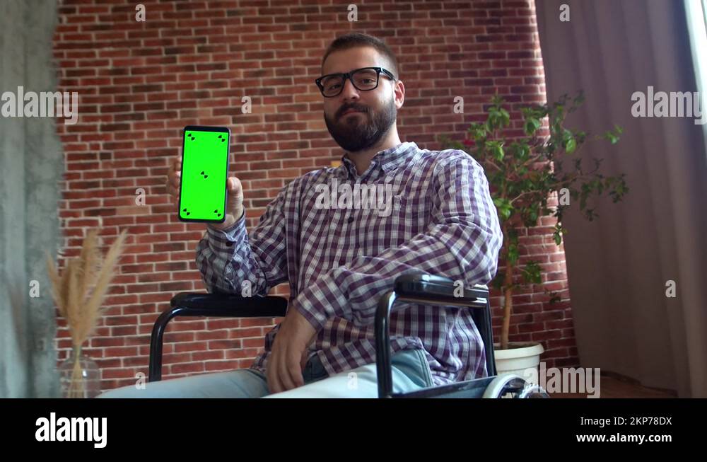Disabled man is sitting in wheelchair and shows green phone screen ...