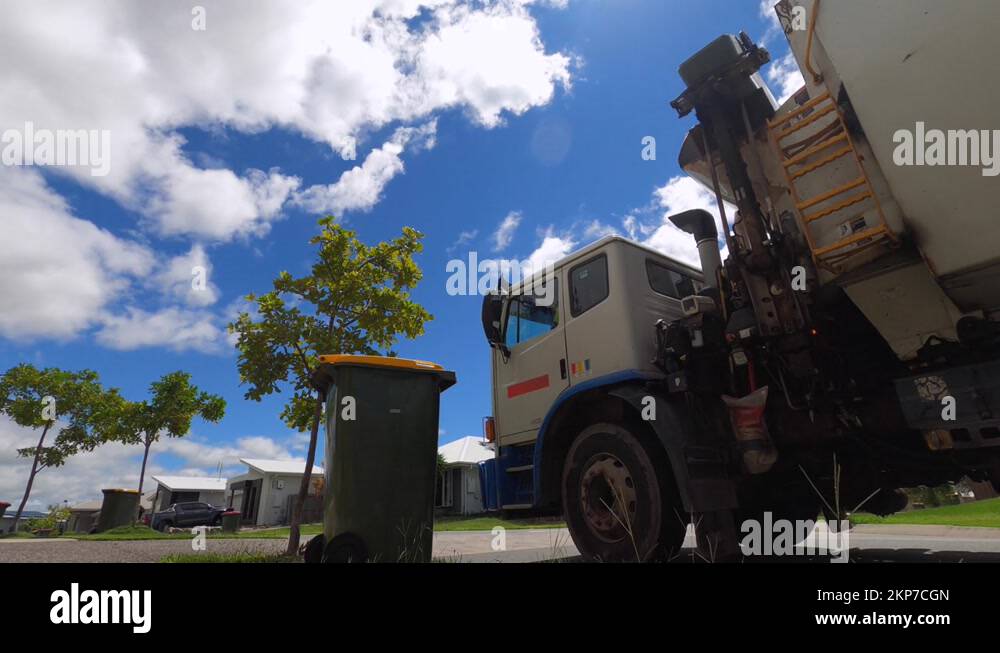 A mechanical arm lifts a wheelie bin and tips rubbish into a garbage ...