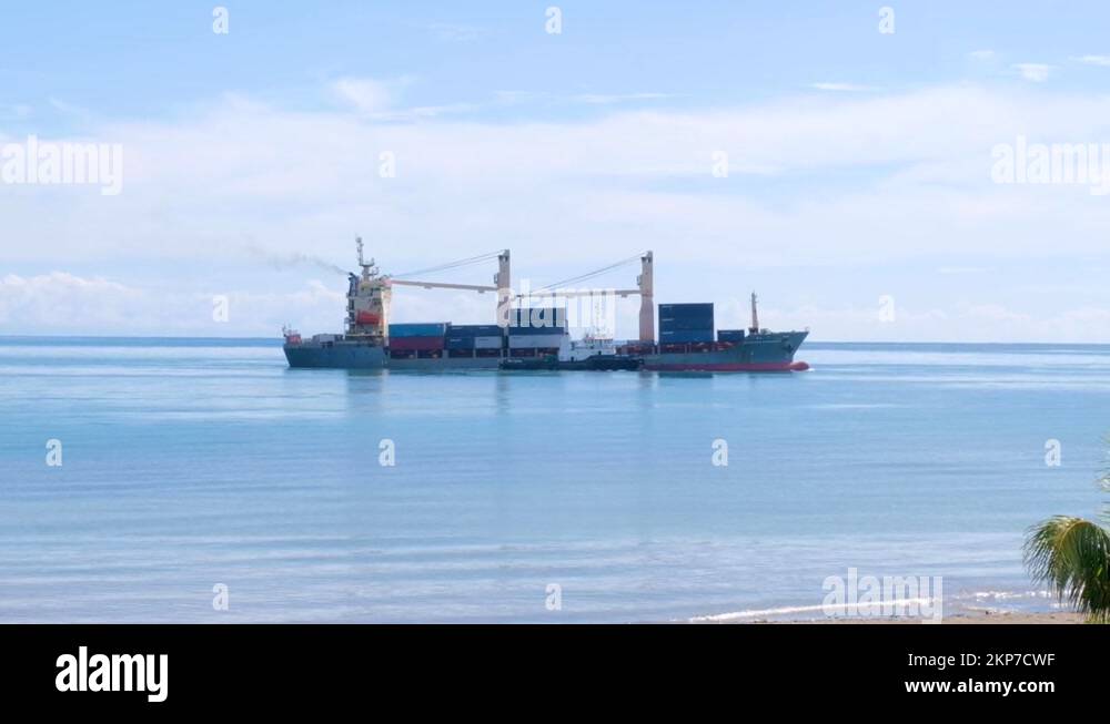 A fully loaded shipping container cargo ship being guided by a tug boat ...