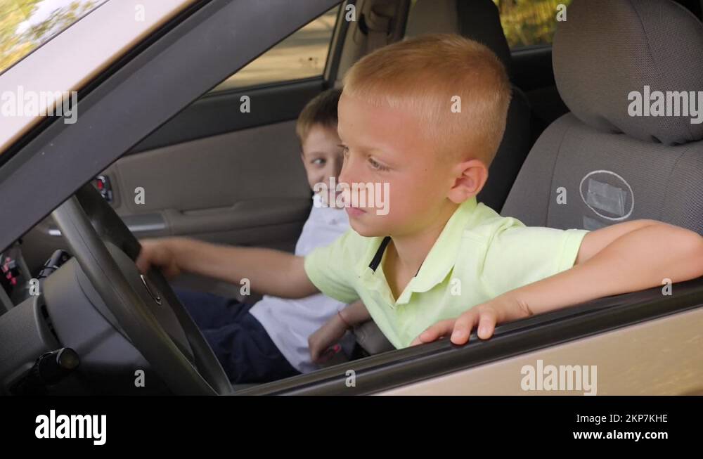 Two boys are sitting behind the wheel of a car and pretending to drive ...