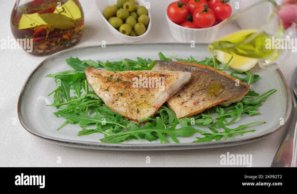 Fried dorado fillet with crispy skin. Woman pouring olive oil on a fish ...