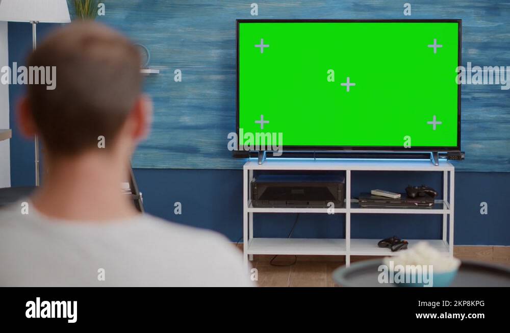 Over shoulder view of man watching movie on tv with green screen ...
