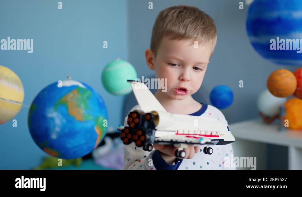 Cute boy is playing with toy space shuttle, flying in space among ...