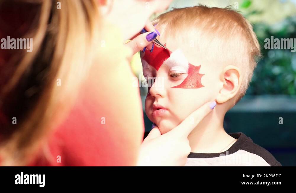 A little boy is put face painting on his face, his face is painted with ...