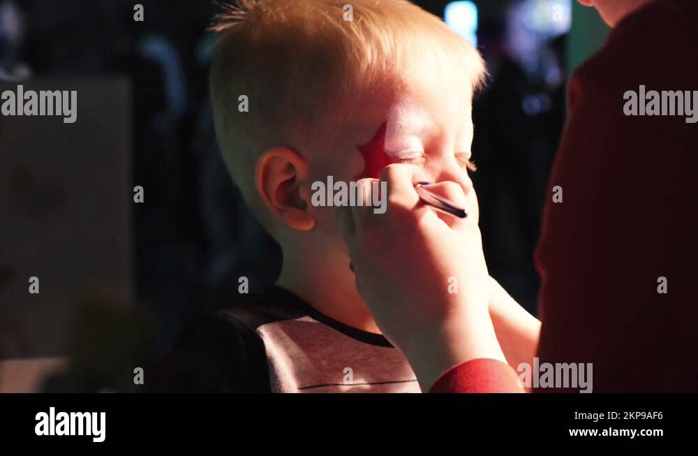 A little boy is put face painting on his face, his face is painted with ...
