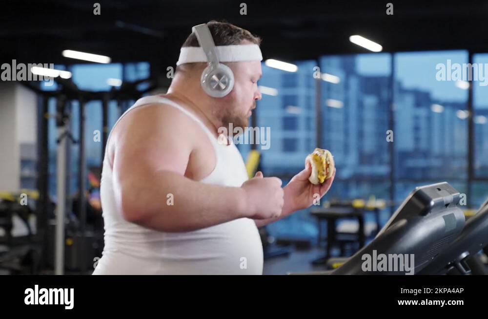 Junk food, overweight funny man run on a treadmill and listening to ...