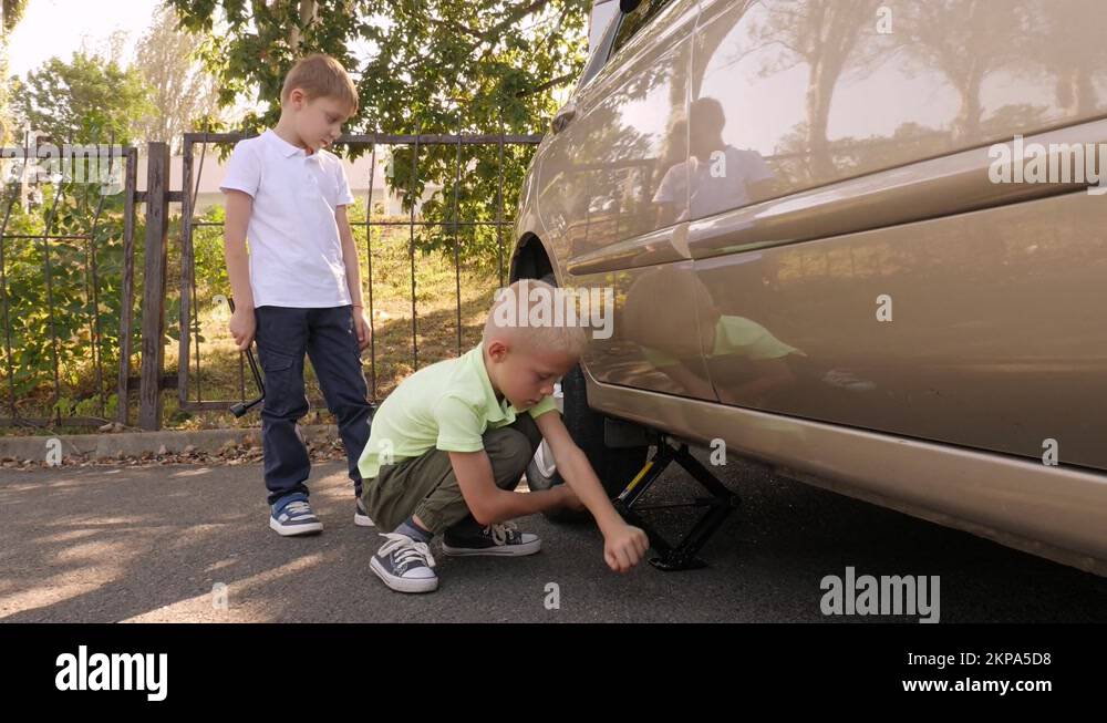 Two curious little boys help Dad fix the car, they lift the car with a ...