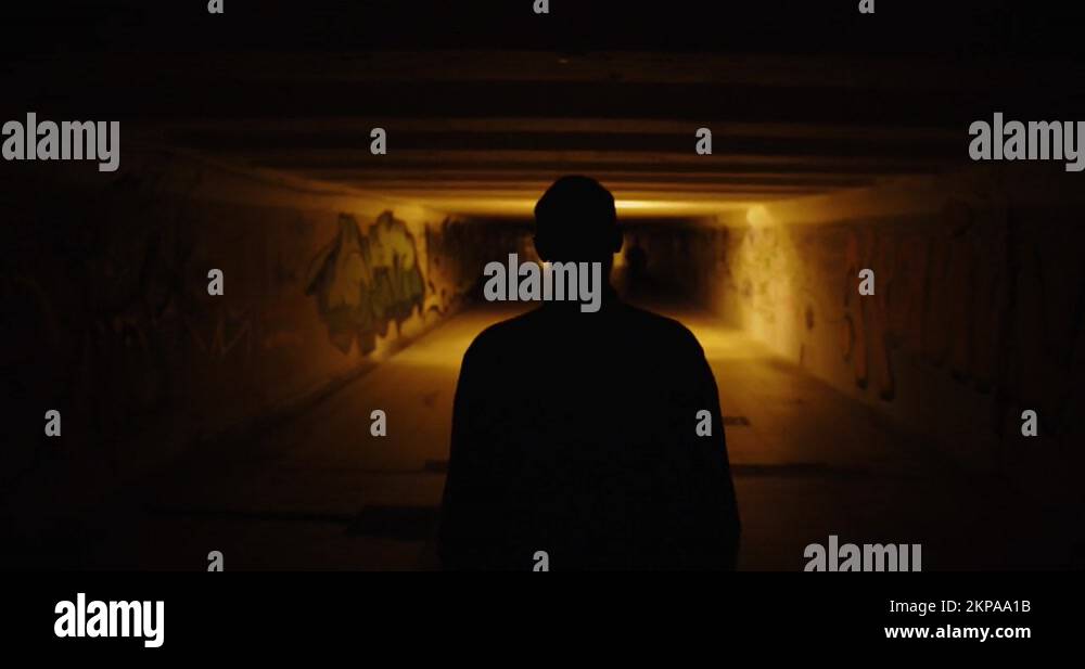 Silhouette of the back of a man walking in a dark underpass. Dark scary ...