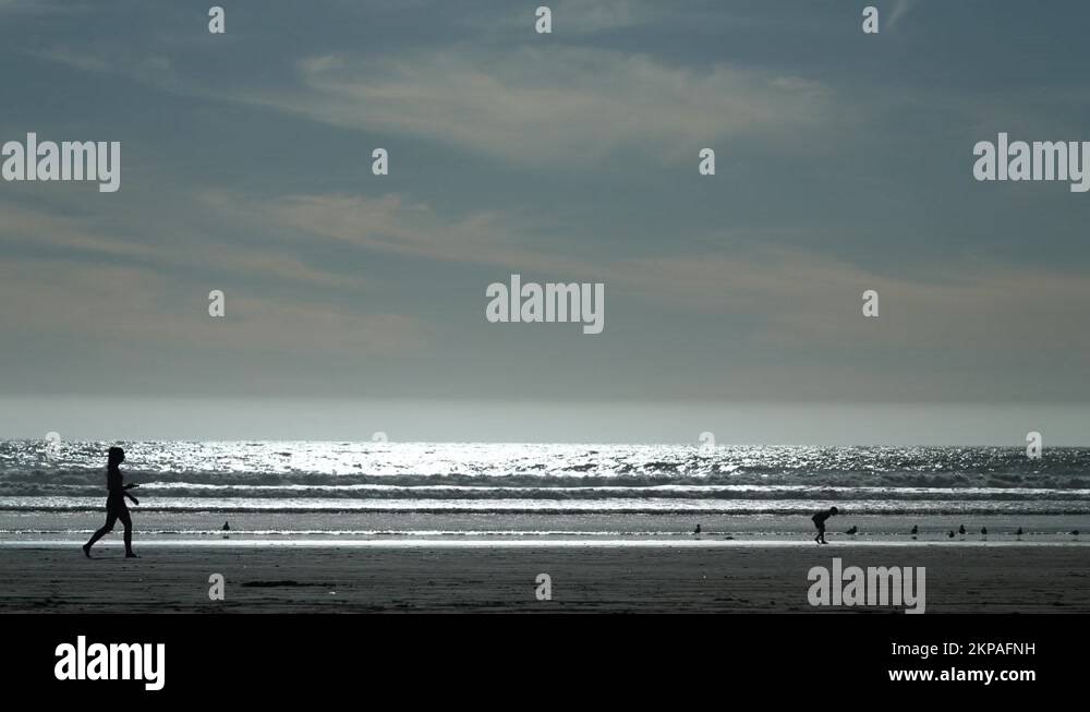Silhouettes of people on the beach - a girl walking and a child ...