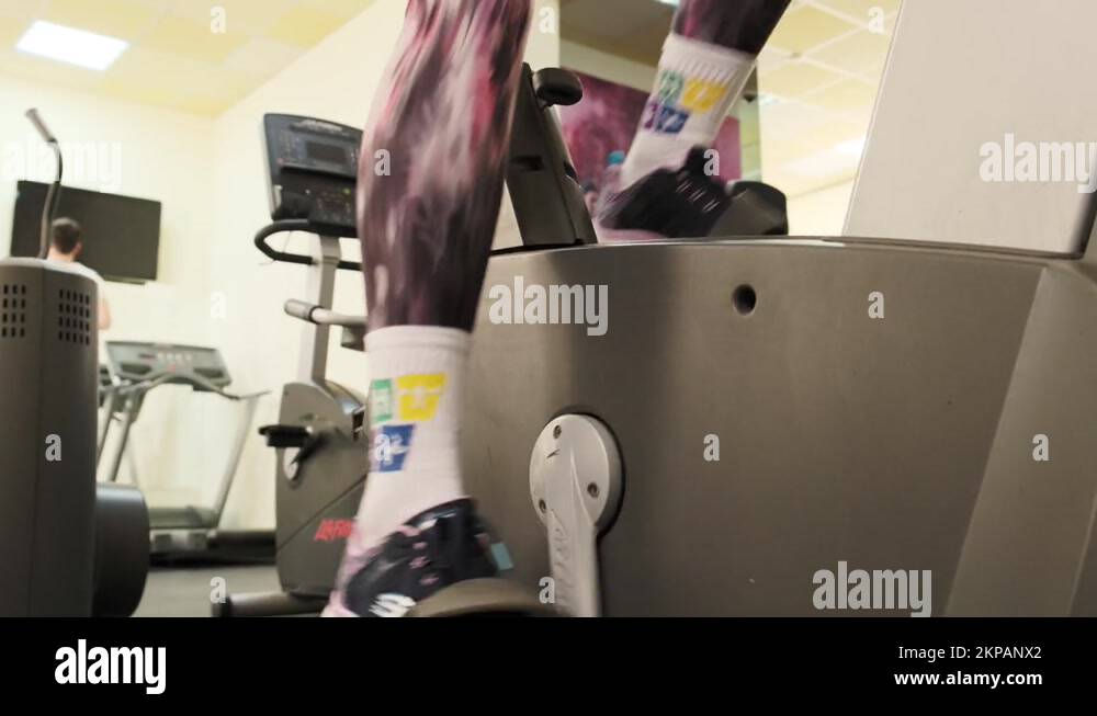 Women's legs in sneakers work on a bike simulator in the gym. Girl ...