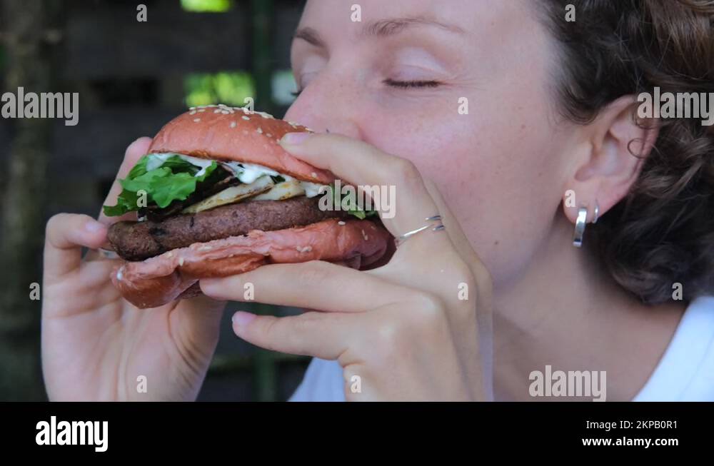 Close-up eating fast food. A white woman takes a big bite from an ...