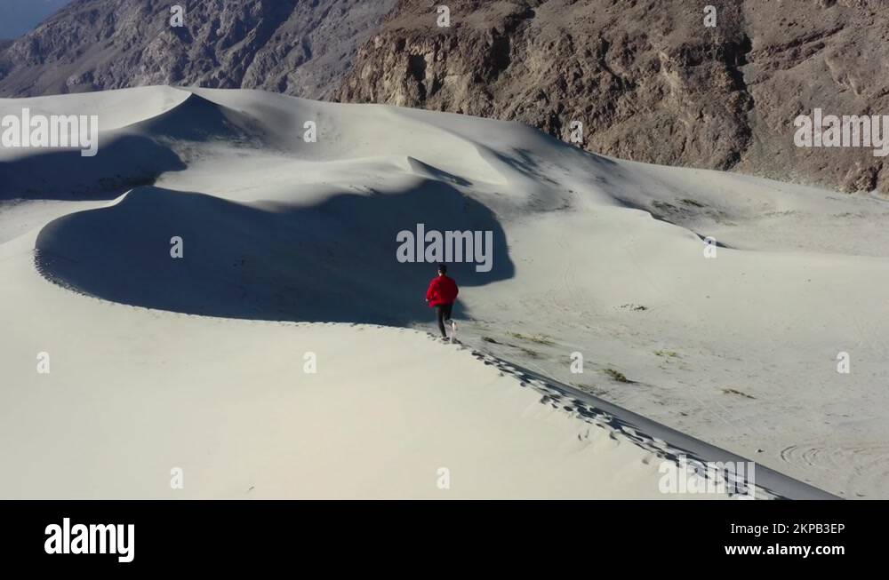 drone tracking a young caucasian male tourist traveling in a red jacket ...