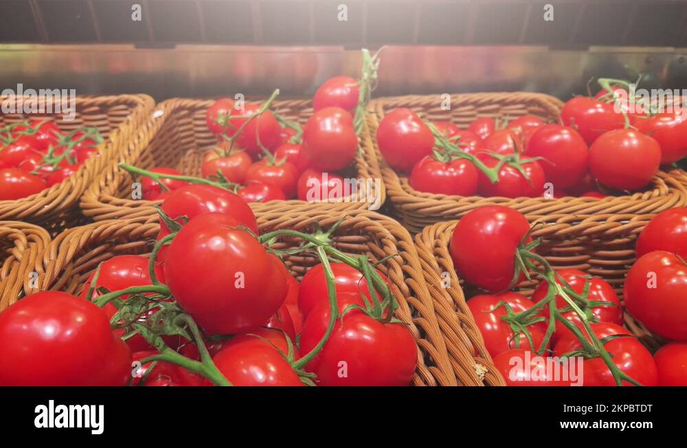 Tomatoes in baskets lie on the shelves of a supermarket or vegetable ...