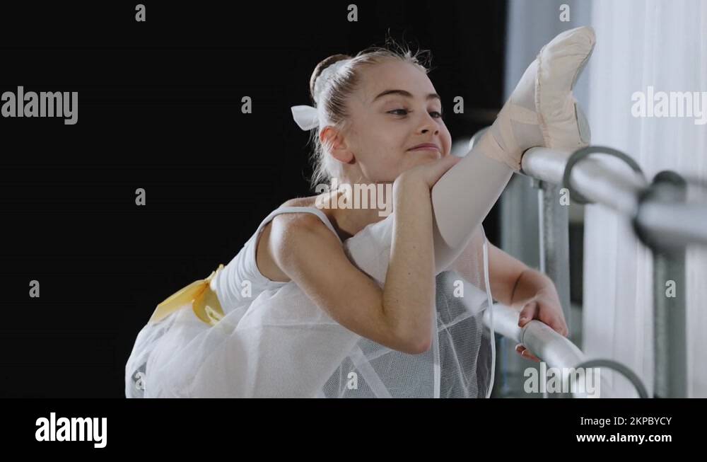 Flexible ballerina girl child in ballet tutu stretches near barre in ...