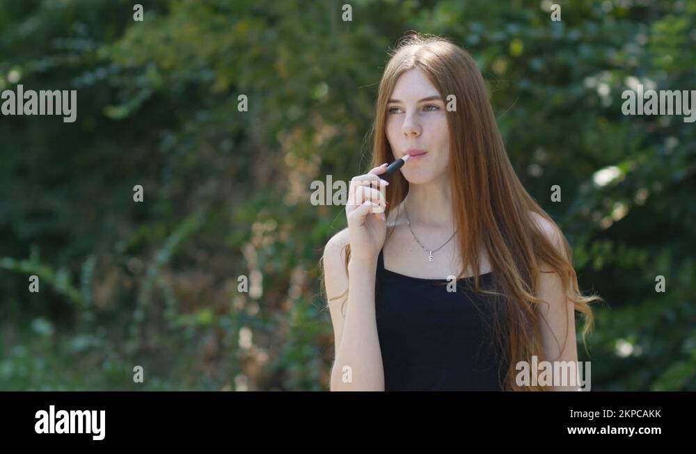 Portrait of a young girl smoking a vape. IQOS. Woman puffs on a vape ...