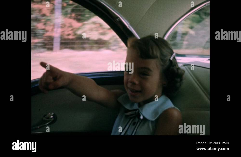 1950s: Girl sitting in back seat of car, smiling, pointing. People ...