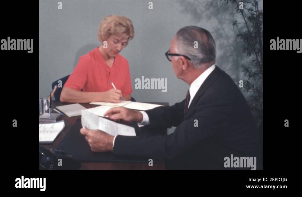 1960s: Secretary sits at business man's desk taking notes. Business man ...
