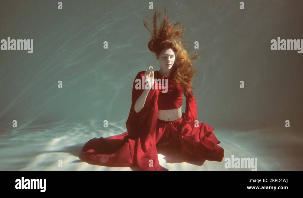 Attractive red-haired young woman swims beautifully underwater in a red ...