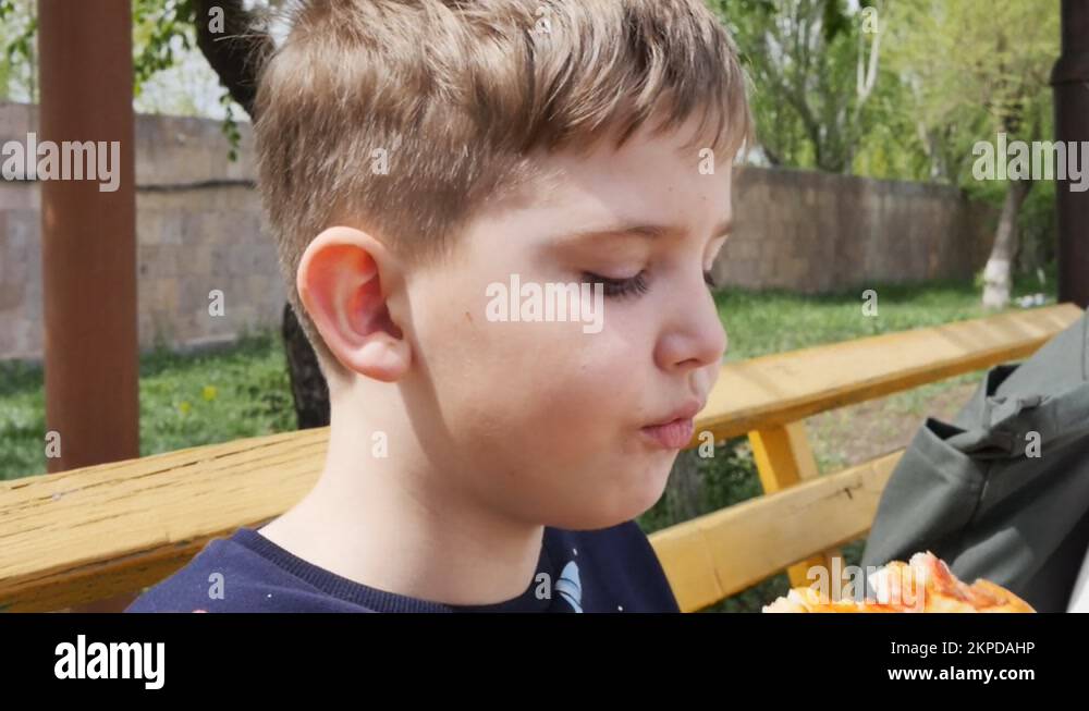 A teenage boy in the park eats a tortilla with cheese and ham. hungry ...