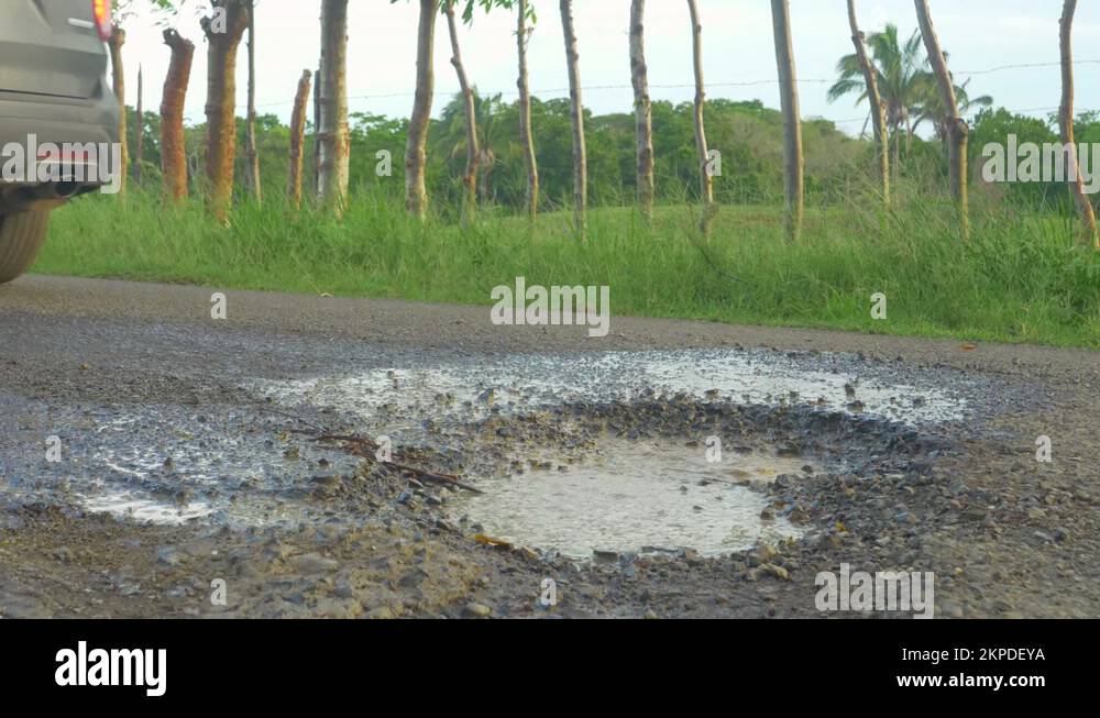 CLOSE UP: Car driving over big road pit puddle and splashing water ...