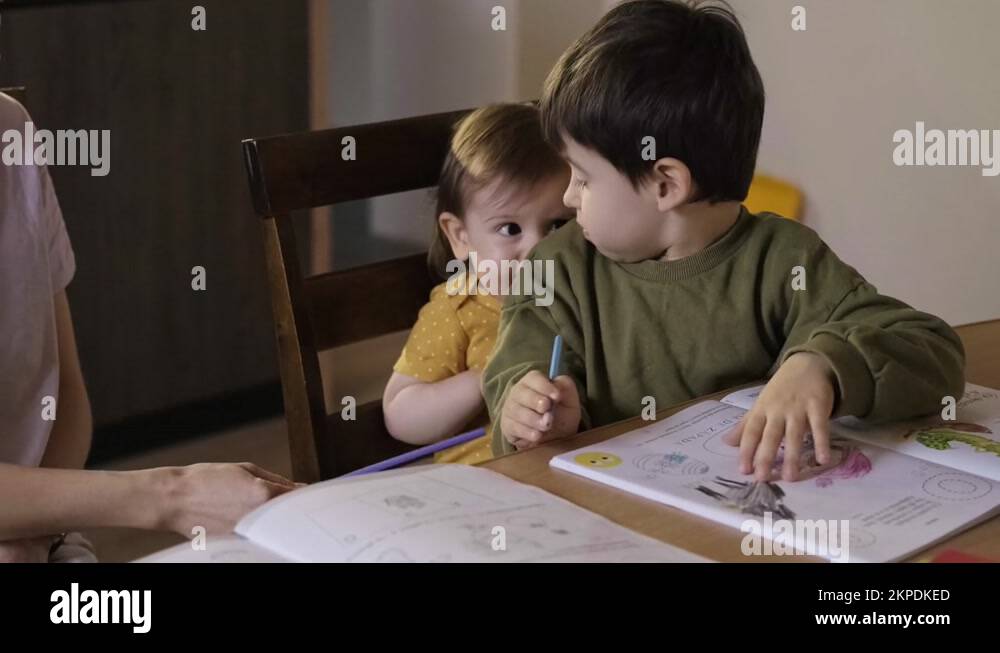 Boy drawing at the lesson table kissing his baby's sister on the ...