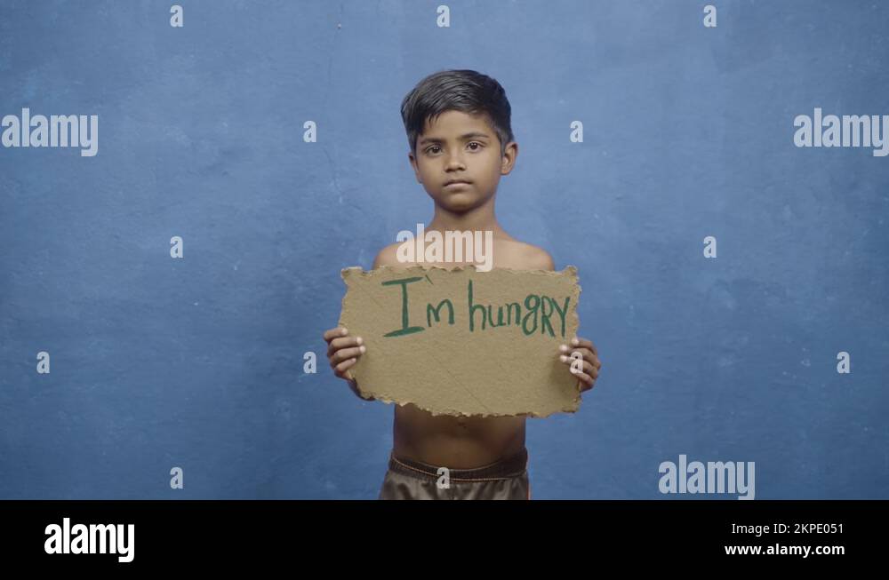 Sad Indian poor kid holding I am hungry sign board by looking at camera ...