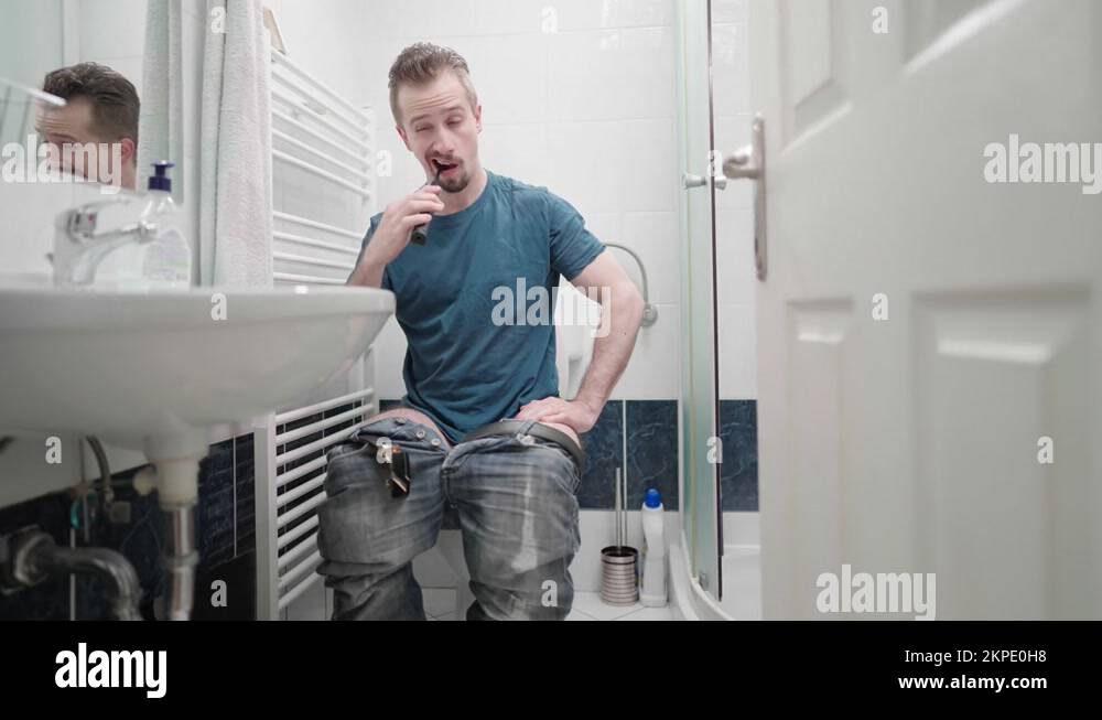 Opening door to bathroom with man on toilet washing teeth multitasking ...