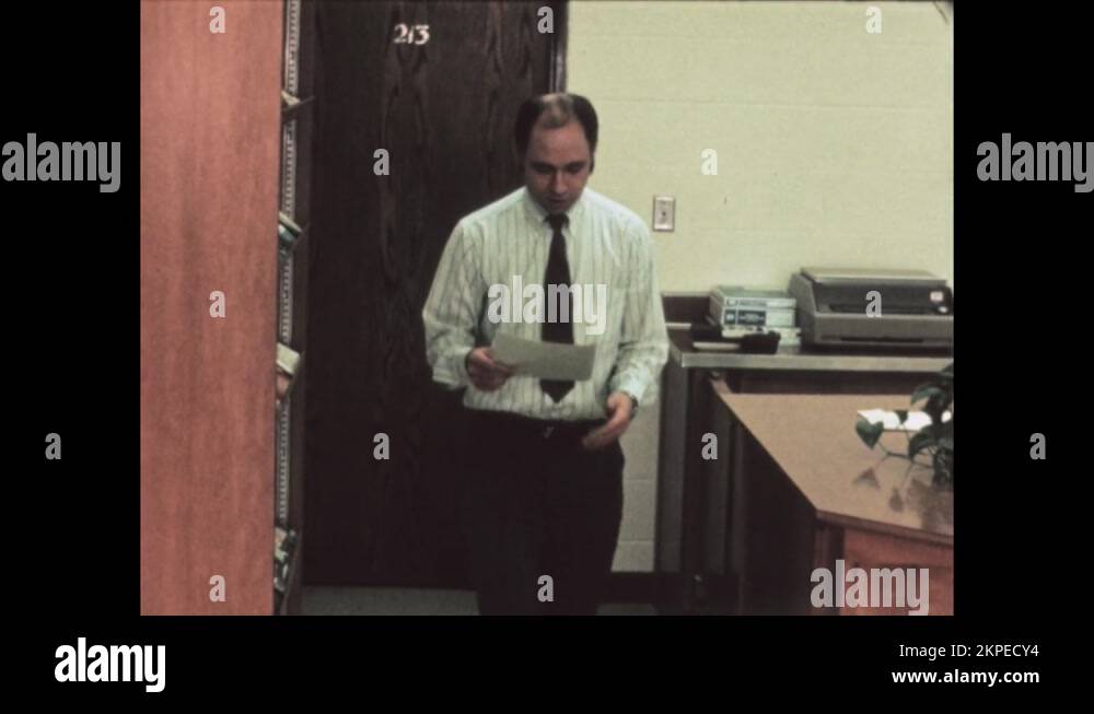 1970s: man reads through notes on paper. Man leaves reception desk. Man ...