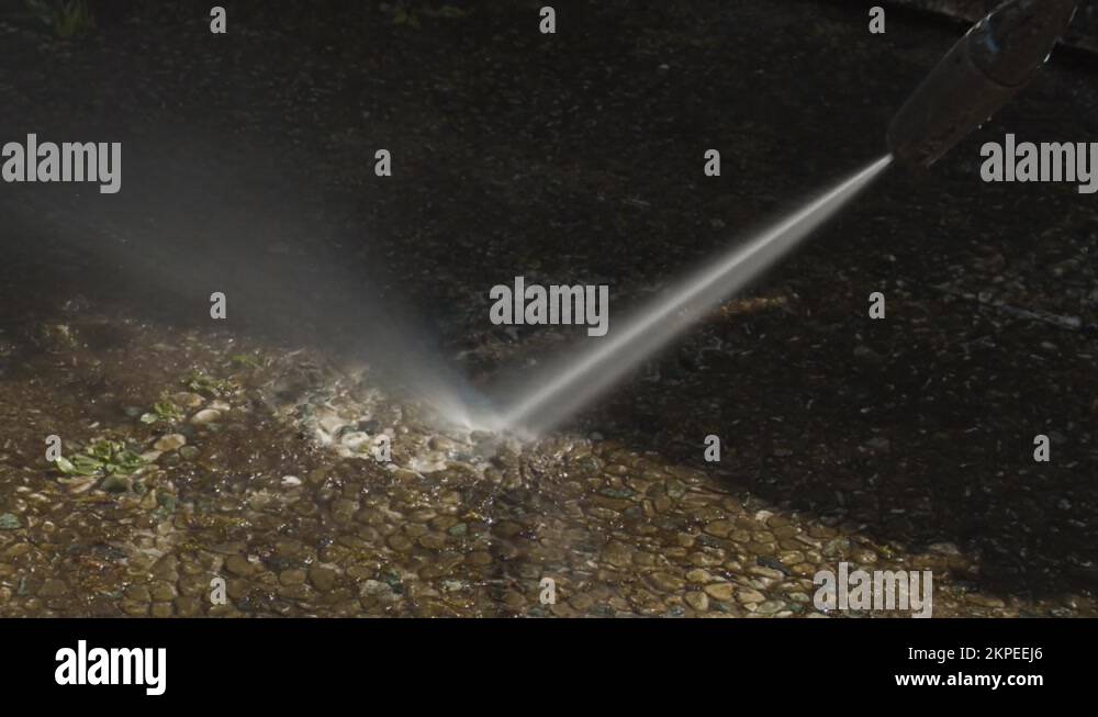 Powerful water jet from pressure washer being sprayed on weed and moss ...