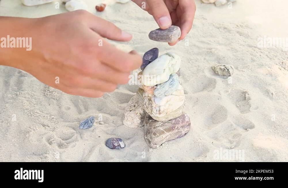 man builds a pyramid of sea stones. heap of smooth pebbles. zen stones ...