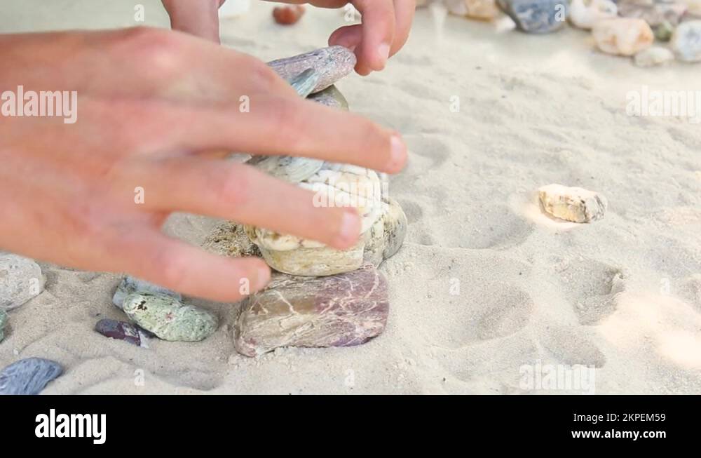 man builds a pyramid of sea stones. heap of smooth pebbles. zen stones ...
