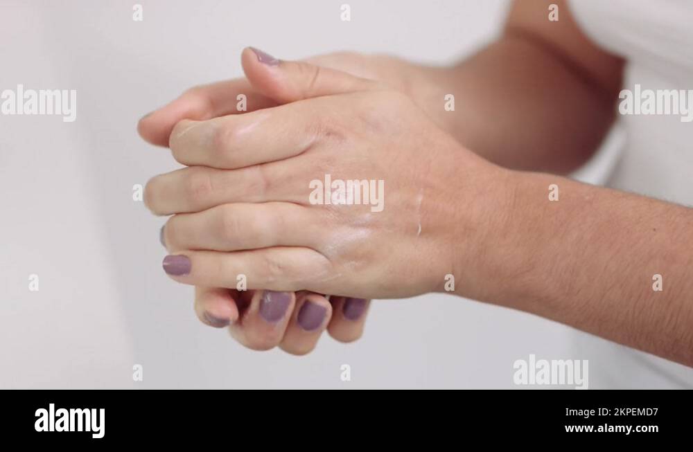 Woman rubs lotion body butter moisturizer on hands wearing white tank ...