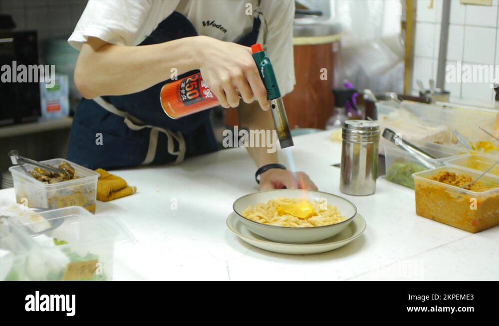 Chef using gas torch to scorch surface of egg and noodle dish in ...